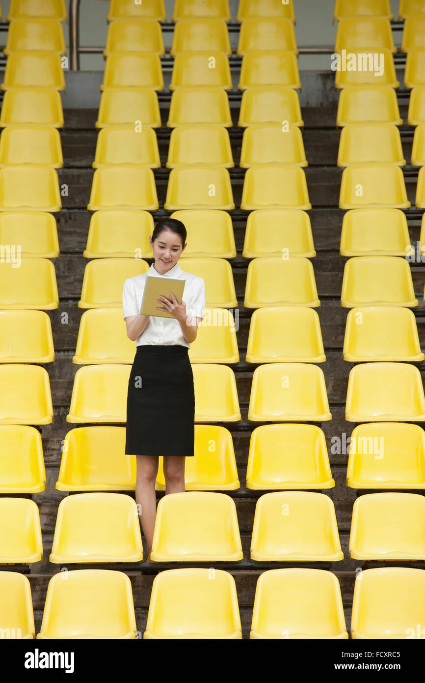 Smiling businesswoman standing and using a tablet at stadium seats ...
