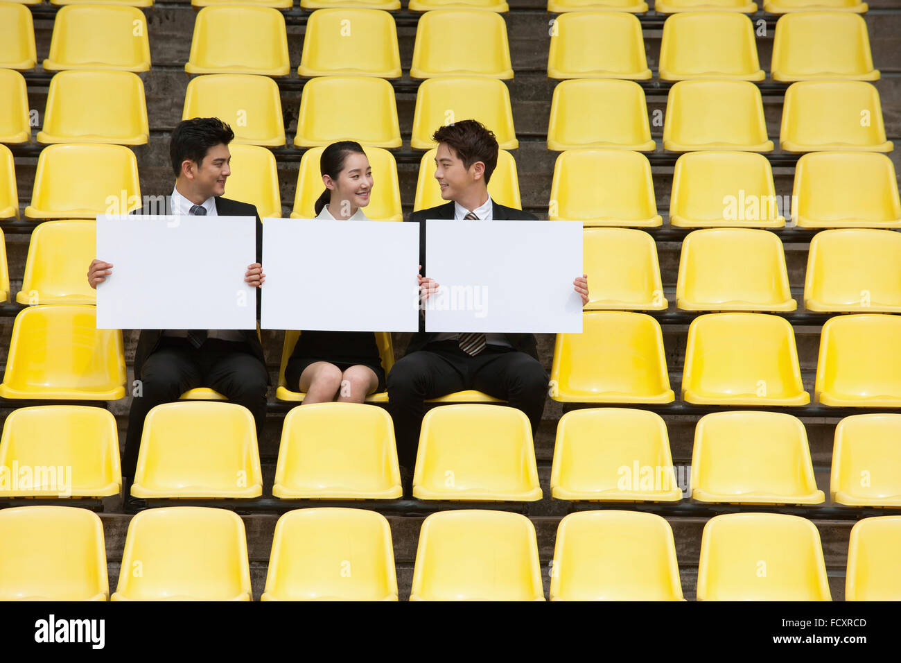 Three business people sitting on stadium seats with papers smiling at ...