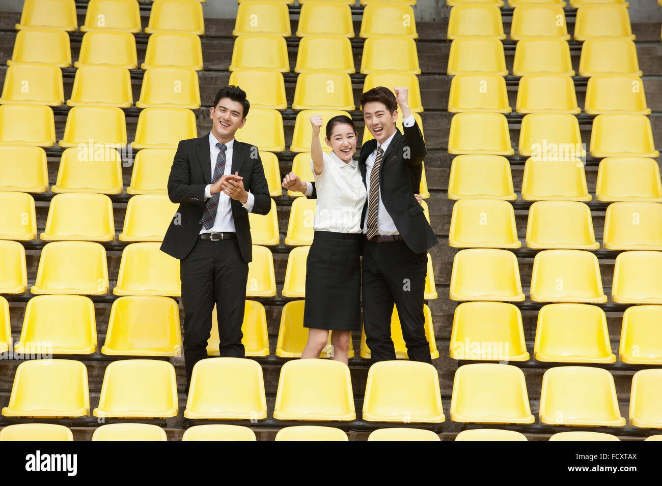 Three young smiling business people standing, clapping and cheering at ...