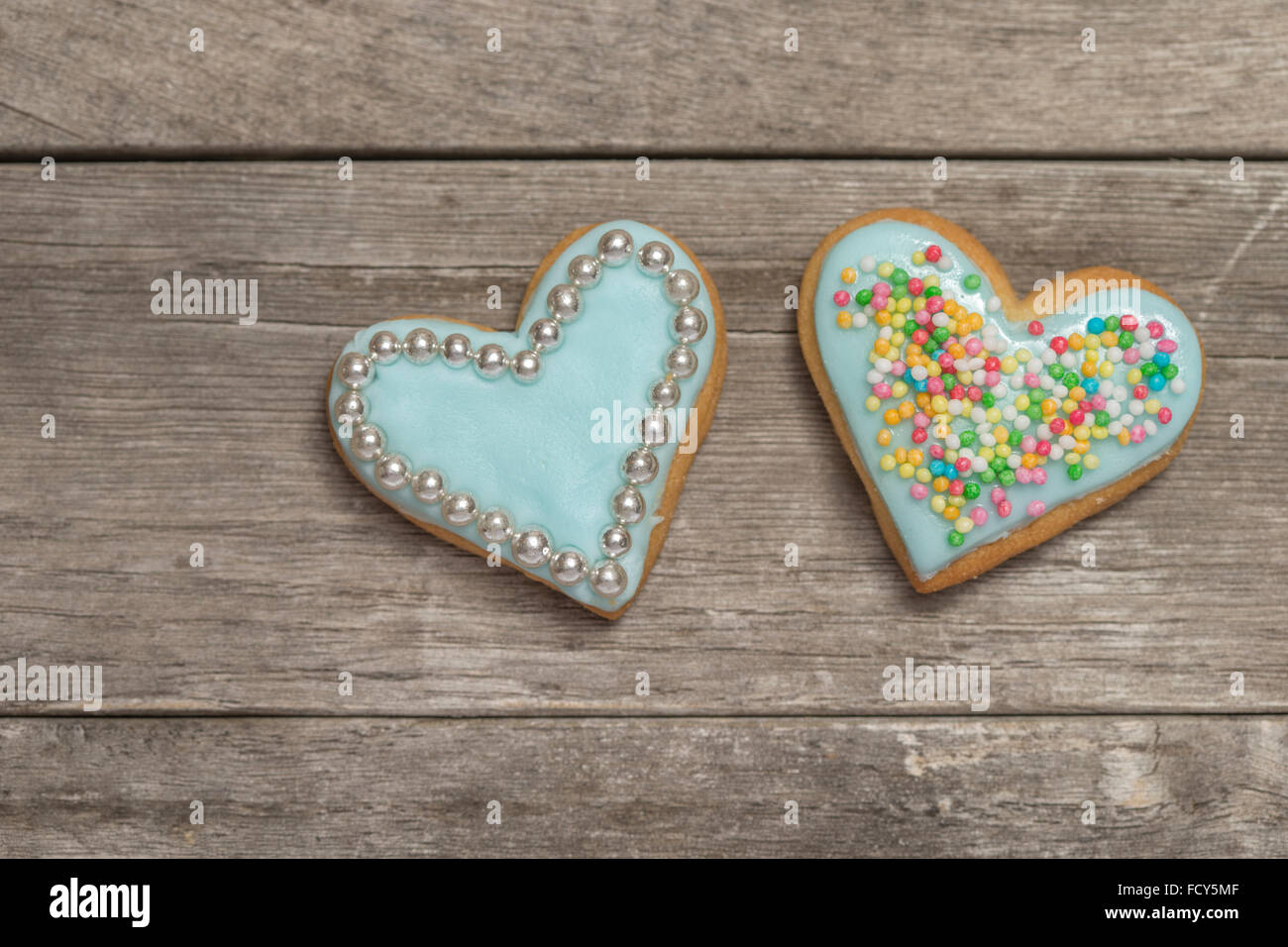Two baked hearts covered with blue icing. Wooden background, from above ...