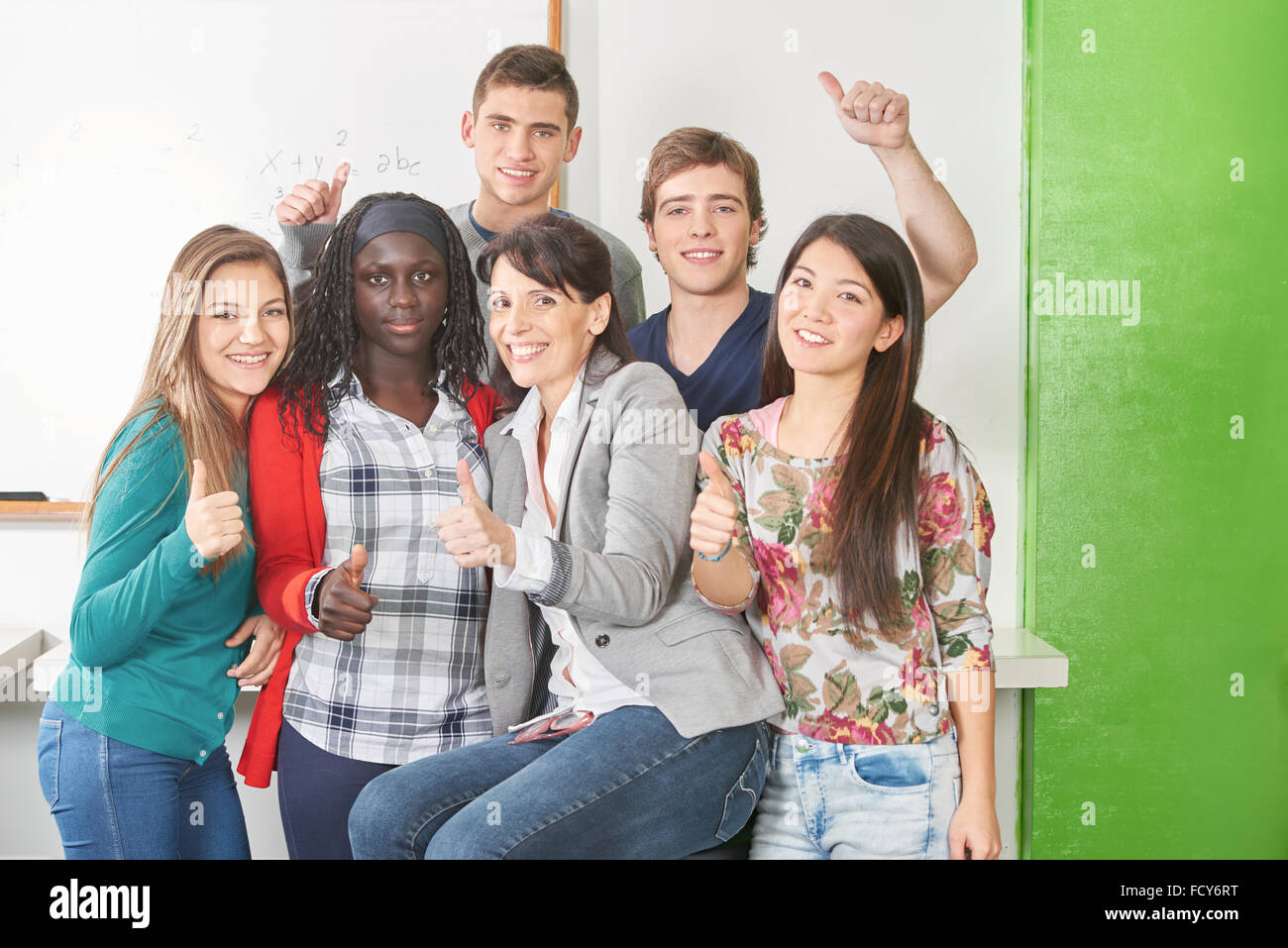 Students and teacher hold their thumbs up in their classroom at their ...