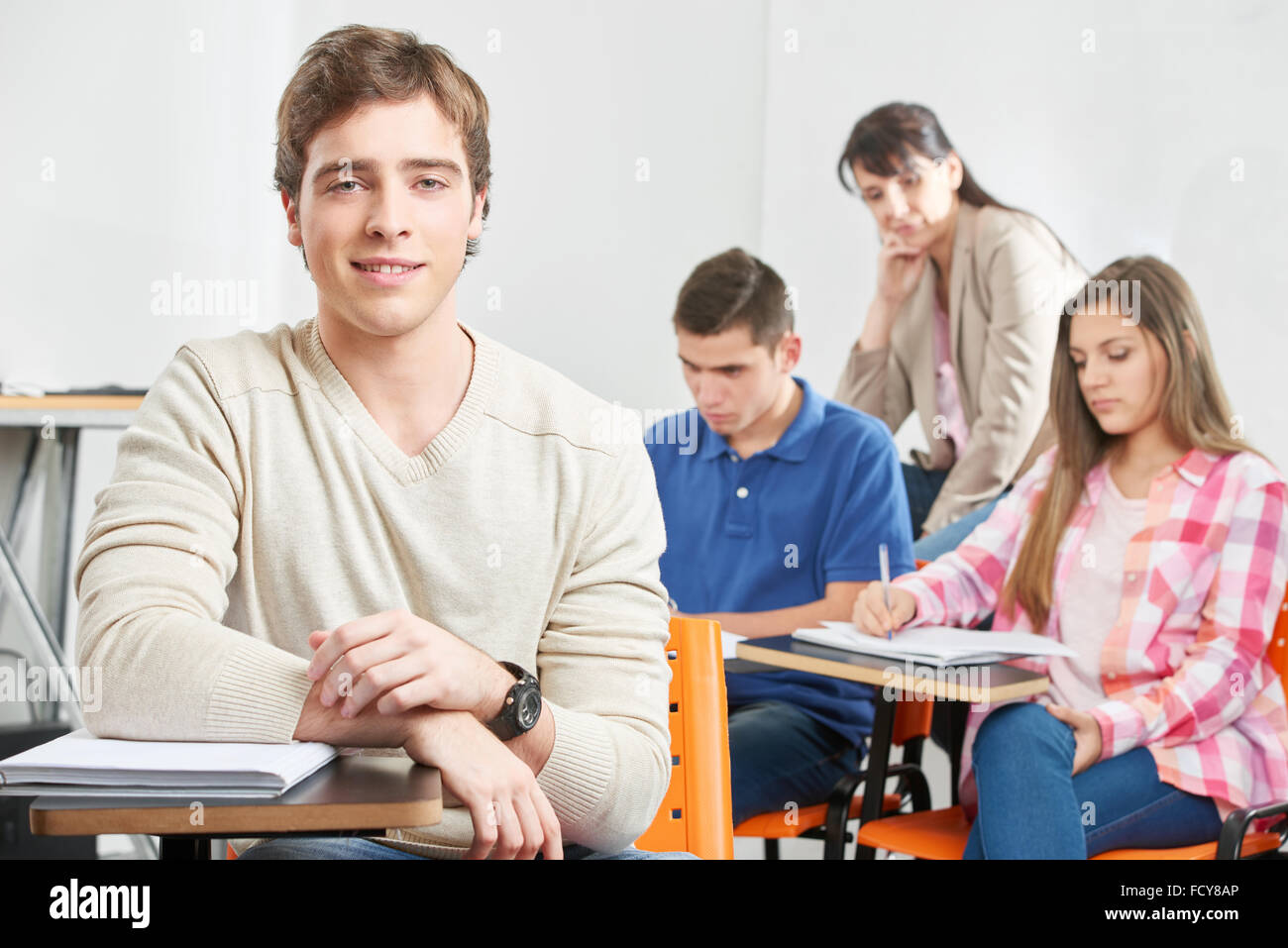 Teenage boy taking a test while his teacher supervises his classmates ...