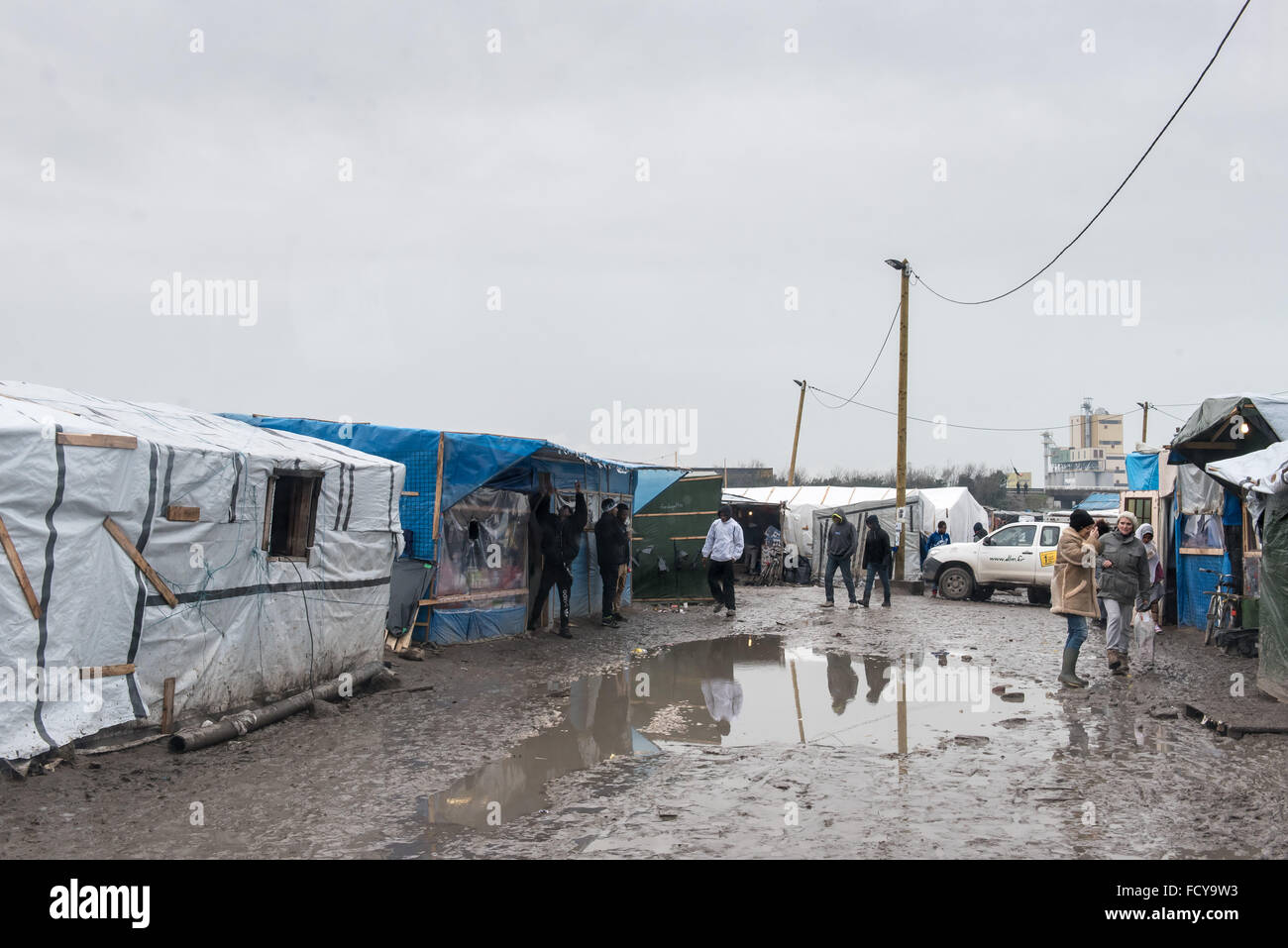 A large pool of water on a track with makeshift shops in the Calais ...