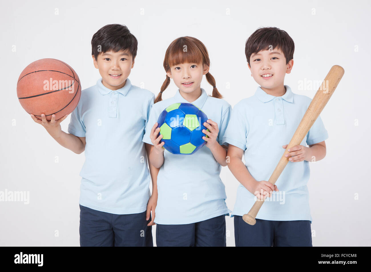 Three elementary school students holding a basketball, a soccer ball ...