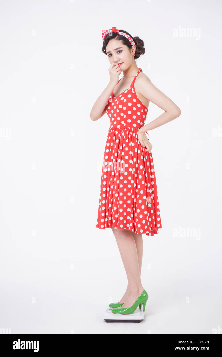 Woman in retro style fashion standing on a scale and making worried ...
