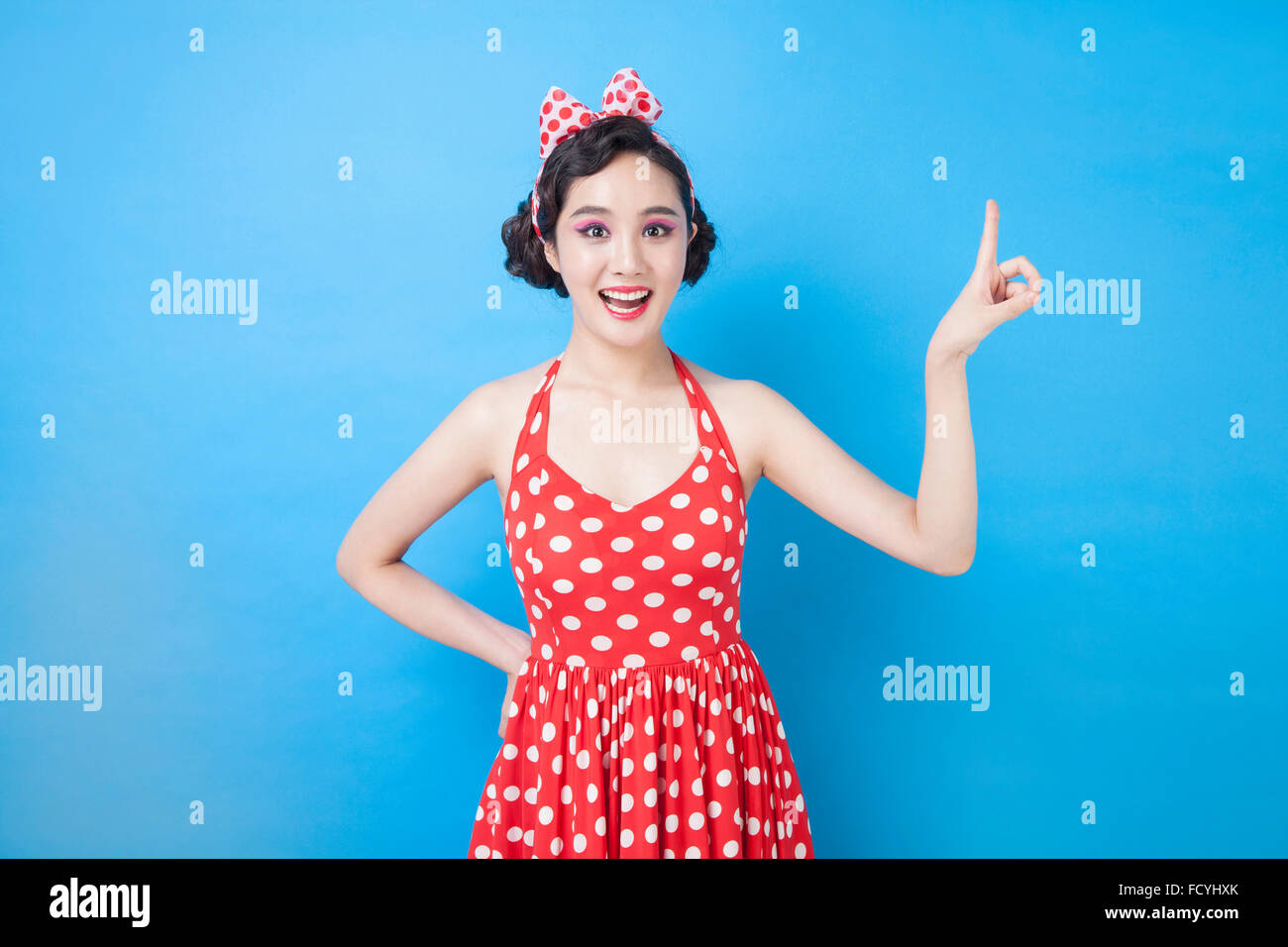 Woman in retro style red dotted dress and hair band pointing up with ...