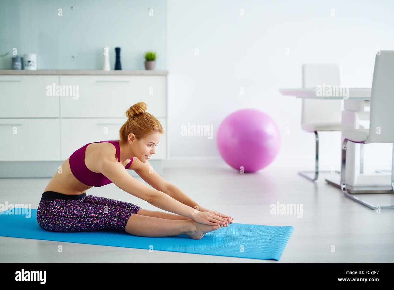 Young woman sitting on mat and doing stretching exercise Stock Photo ...