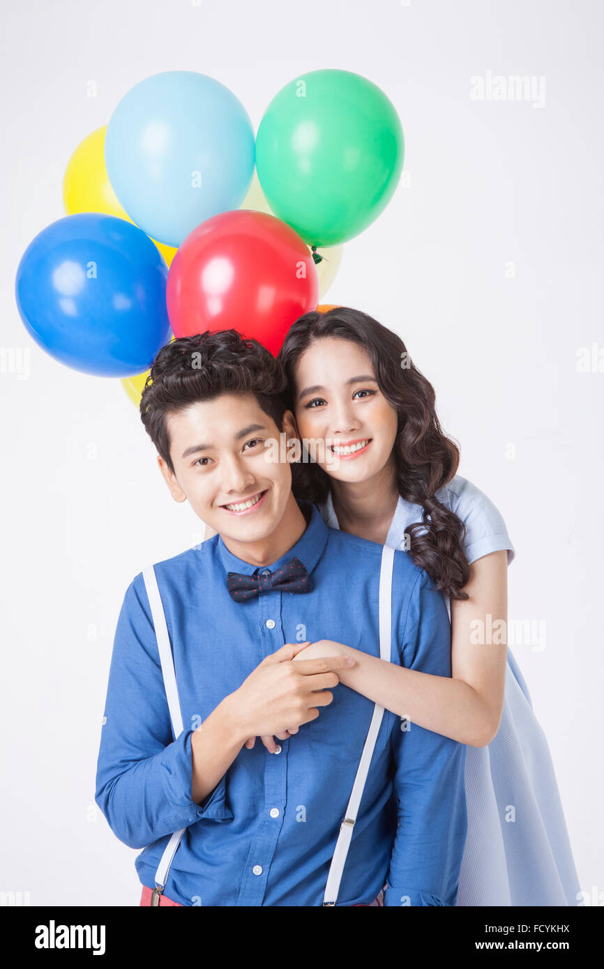 Woman with colorful balloons hugging from behind a man and both in ...