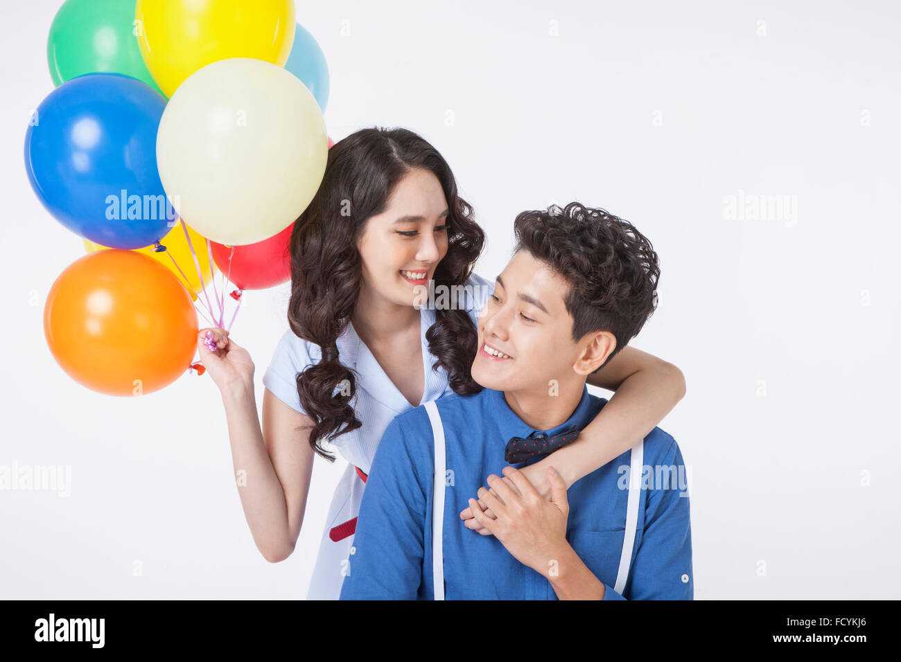 Woman with colorful balloons hugging from behind a man and both looking ...