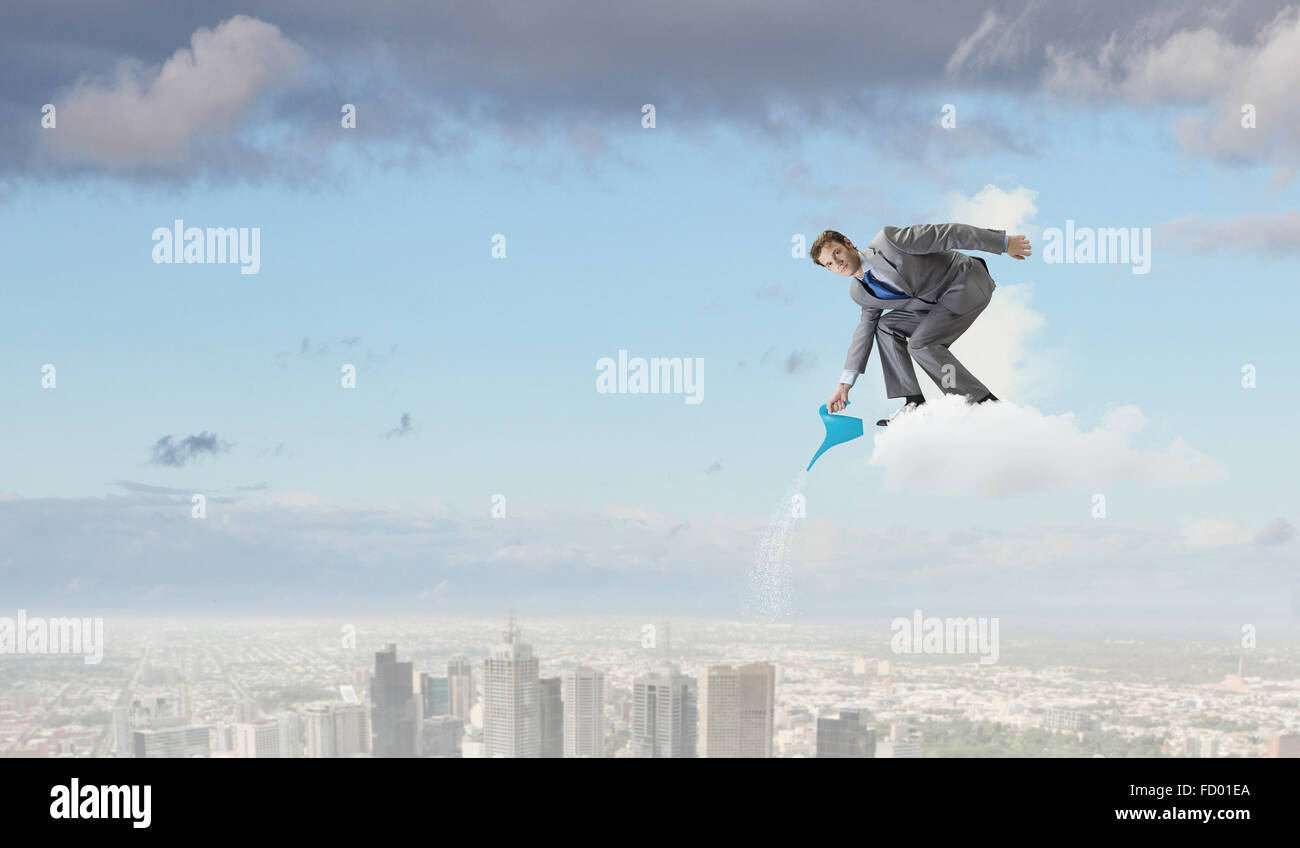 Young businessman standing on cloud and watering something below Stock ...