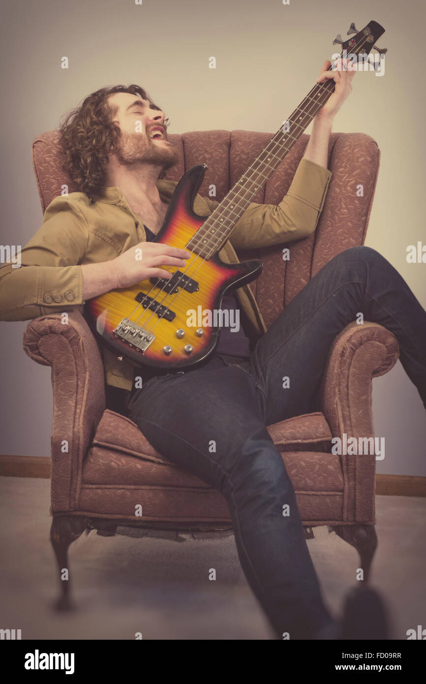 Bearded musician playing electric bass guitar in vintage chair Stock ...