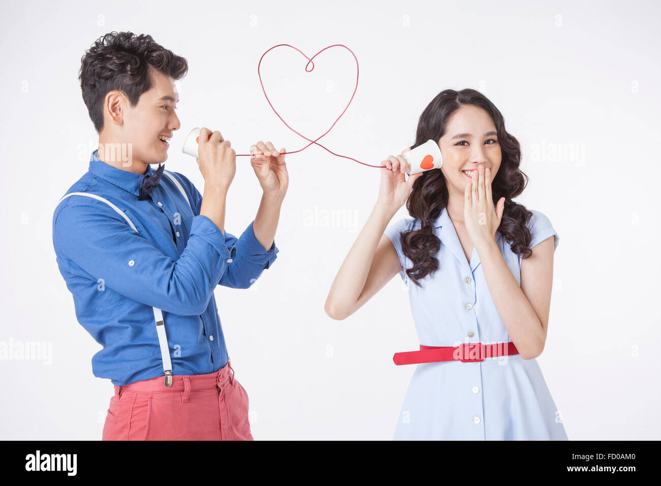 Young adult couple in retro style holding a thread phone making a heart ...