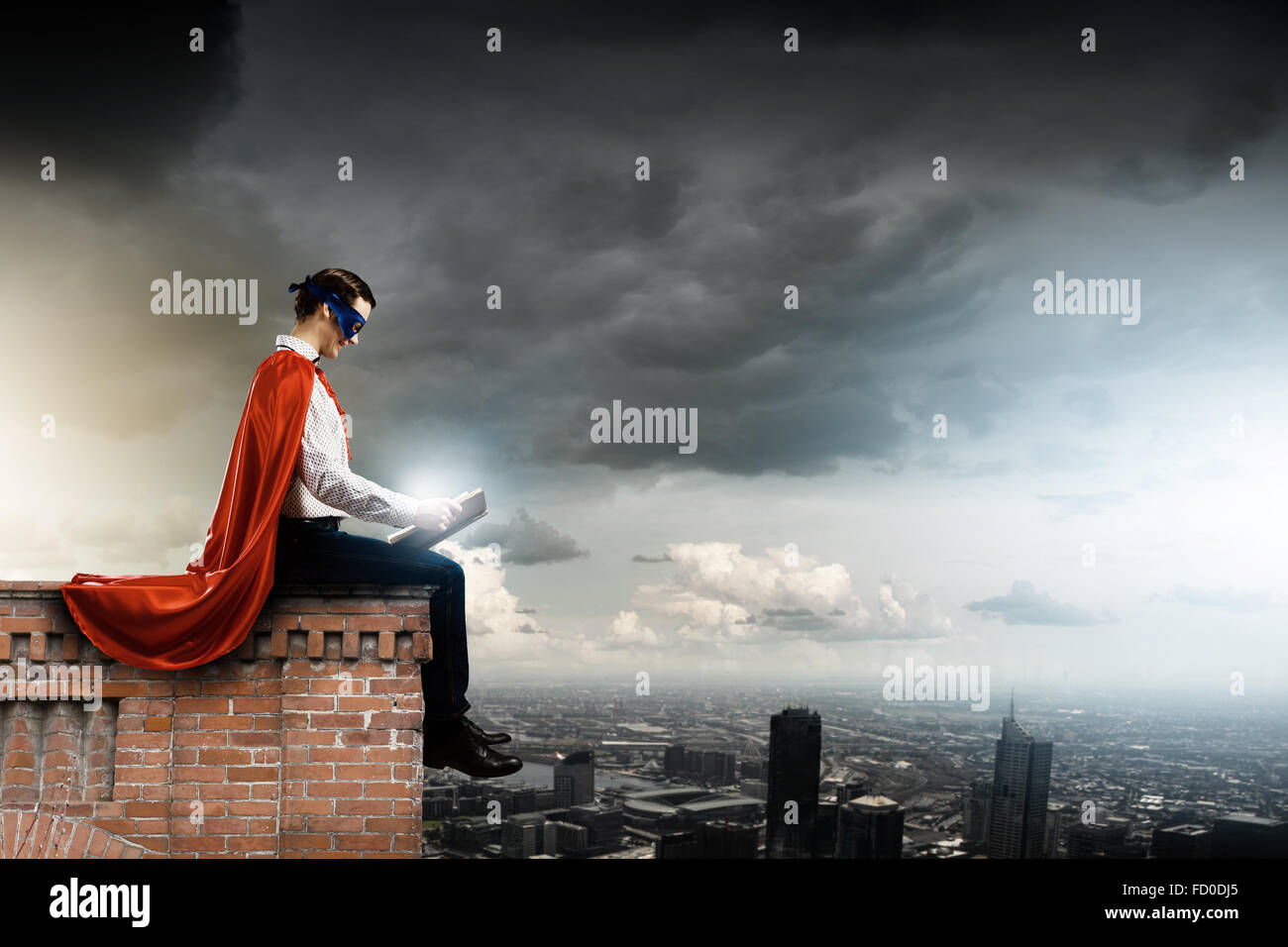 Superman in cape and mask sitting on top of building and reading book ...