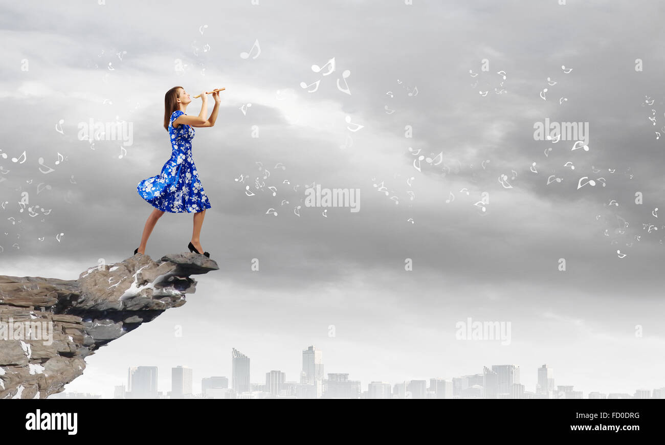 Young woman in blue dress on edge of rock playing fife Stock Photo - Alamy