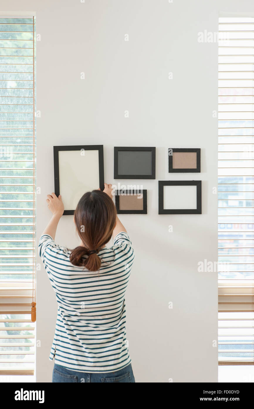 Back appearance of a woman hanging frames on the wall Stock Photo - Alamy