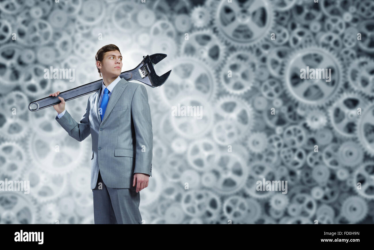 Young determined businessman with wrench on shoulder and cogwheels at ...