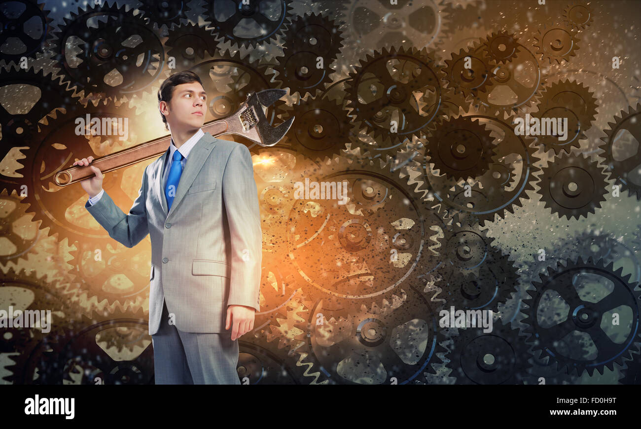 Young determined businessman with wrench on shoulder and cogwheels at ...
