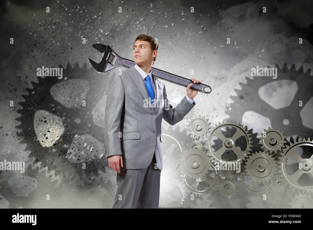 Young determined businessman with wrench on shoulder and cogwheels at ...