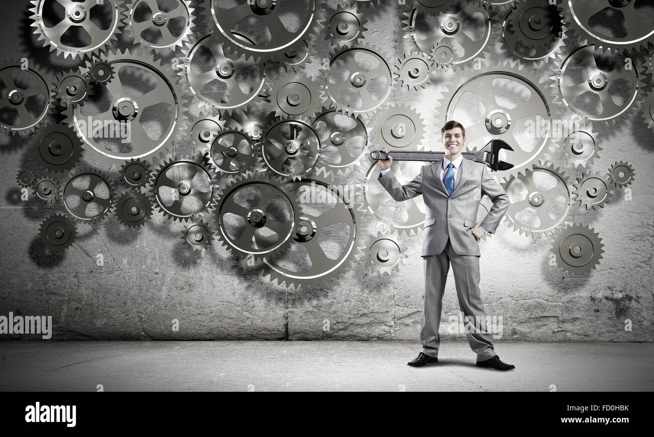 Young determined businessman with wrench on shoulder and cogwheels at ...