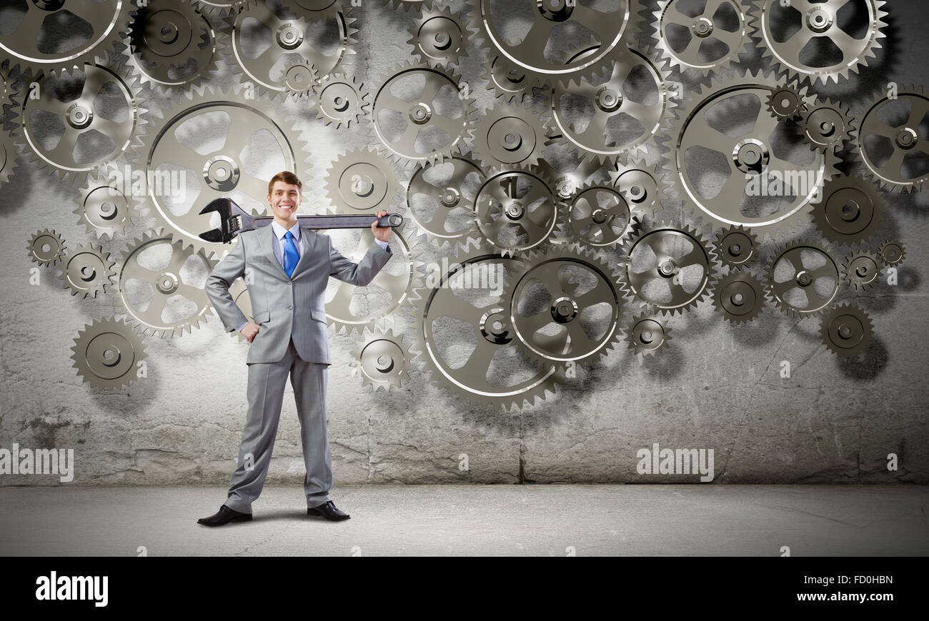 Young determined businessman with wrench on shoulder and cogwheels at ...