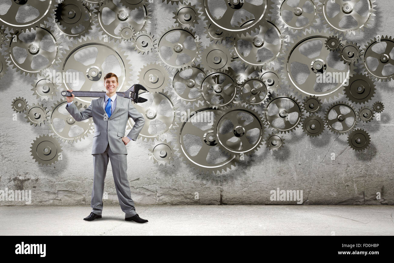 Young determined businessman with wrench on shoulder and cogwheels at ...
