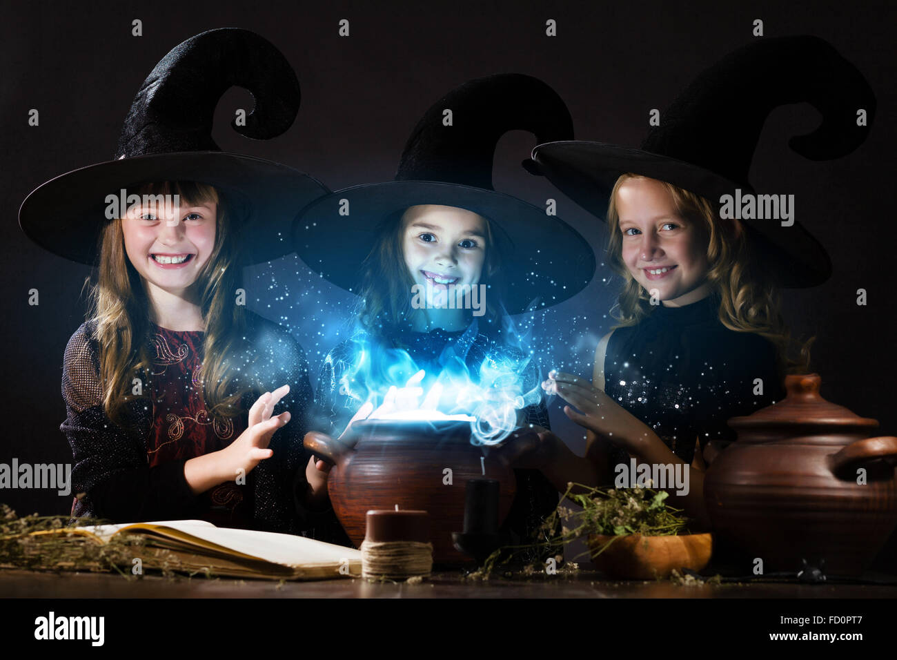 Three little Halloween witches reading spell above pot Stock Photo - Alamy
