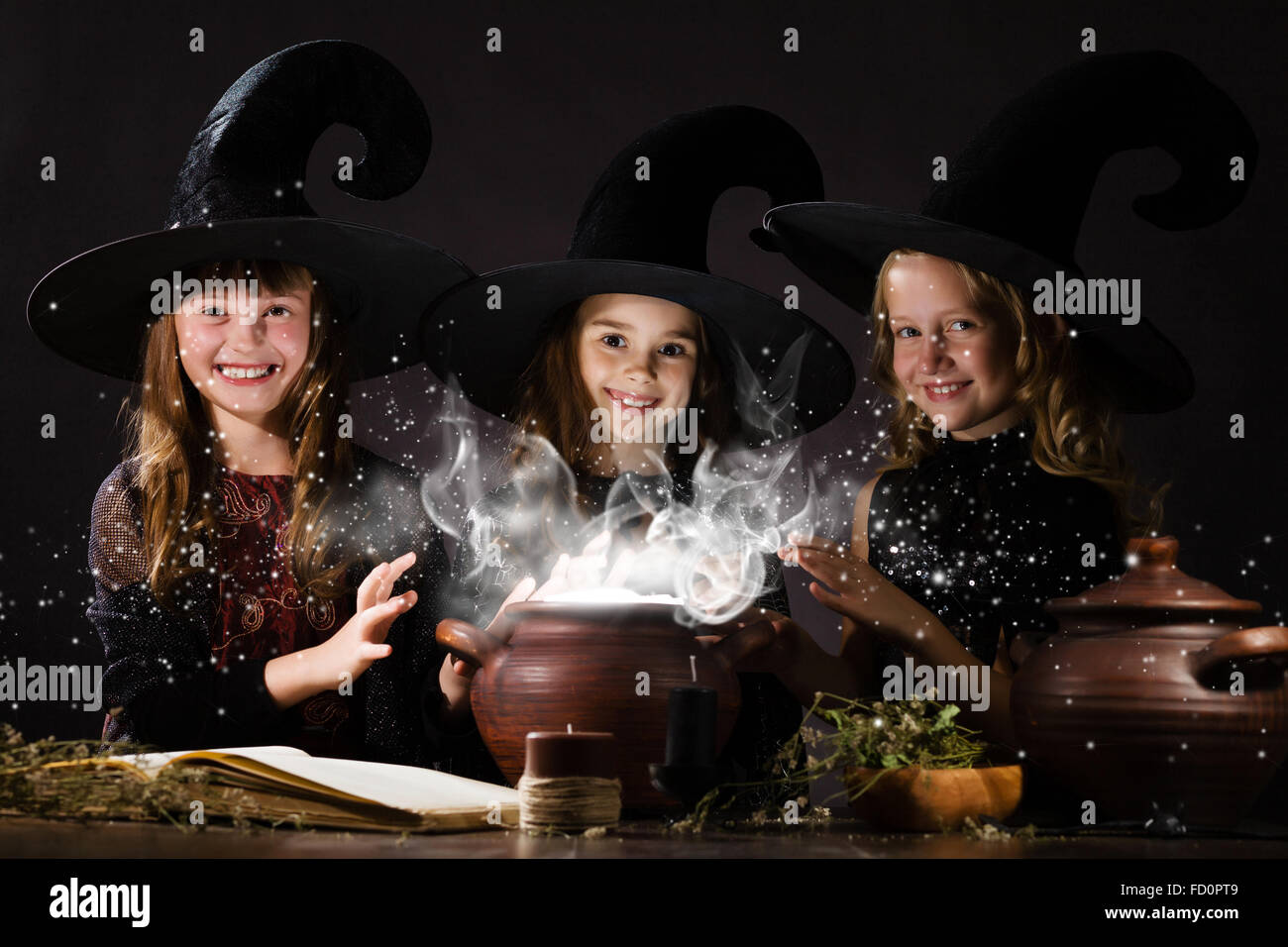 Three little Halloween witches reading spell above pot Stock Photo - Alamy