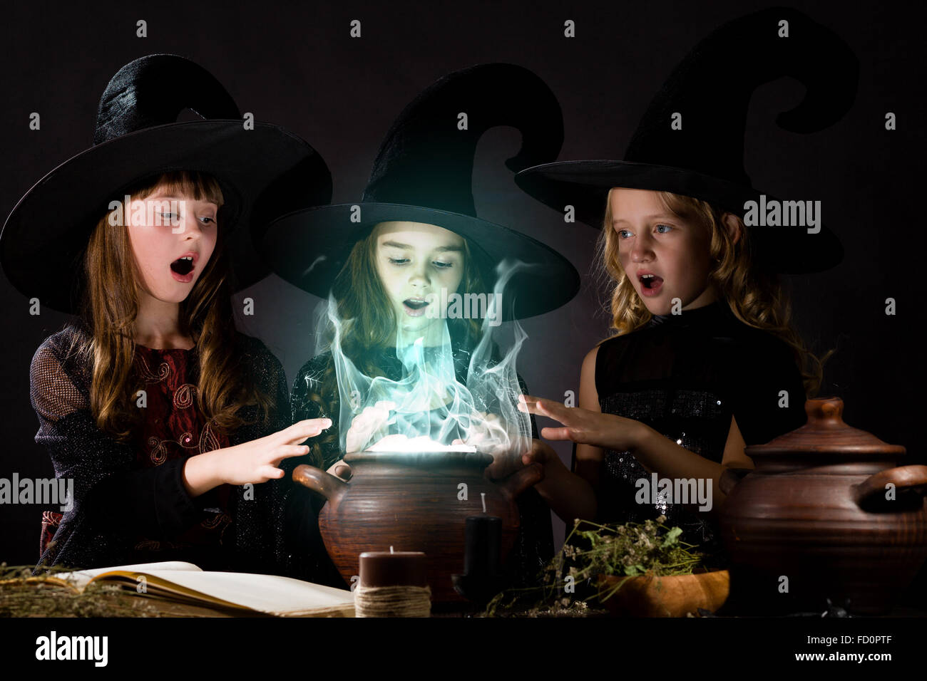 Three little Halloween witches reading spell above pot Stock Photo - Alamy