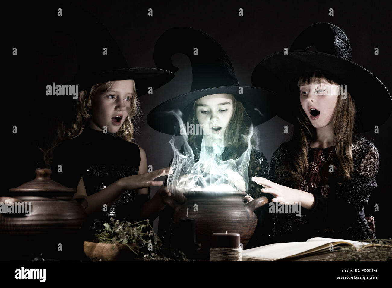 Three little Halloween witches reading spell above pot Stock Photo - Alamy