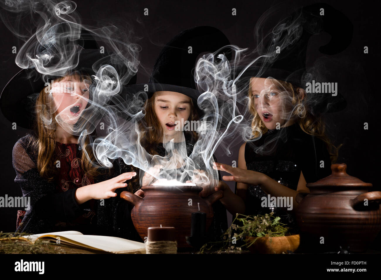 Three little Halloween witches reading spell above pot Stock Photo - Alamy