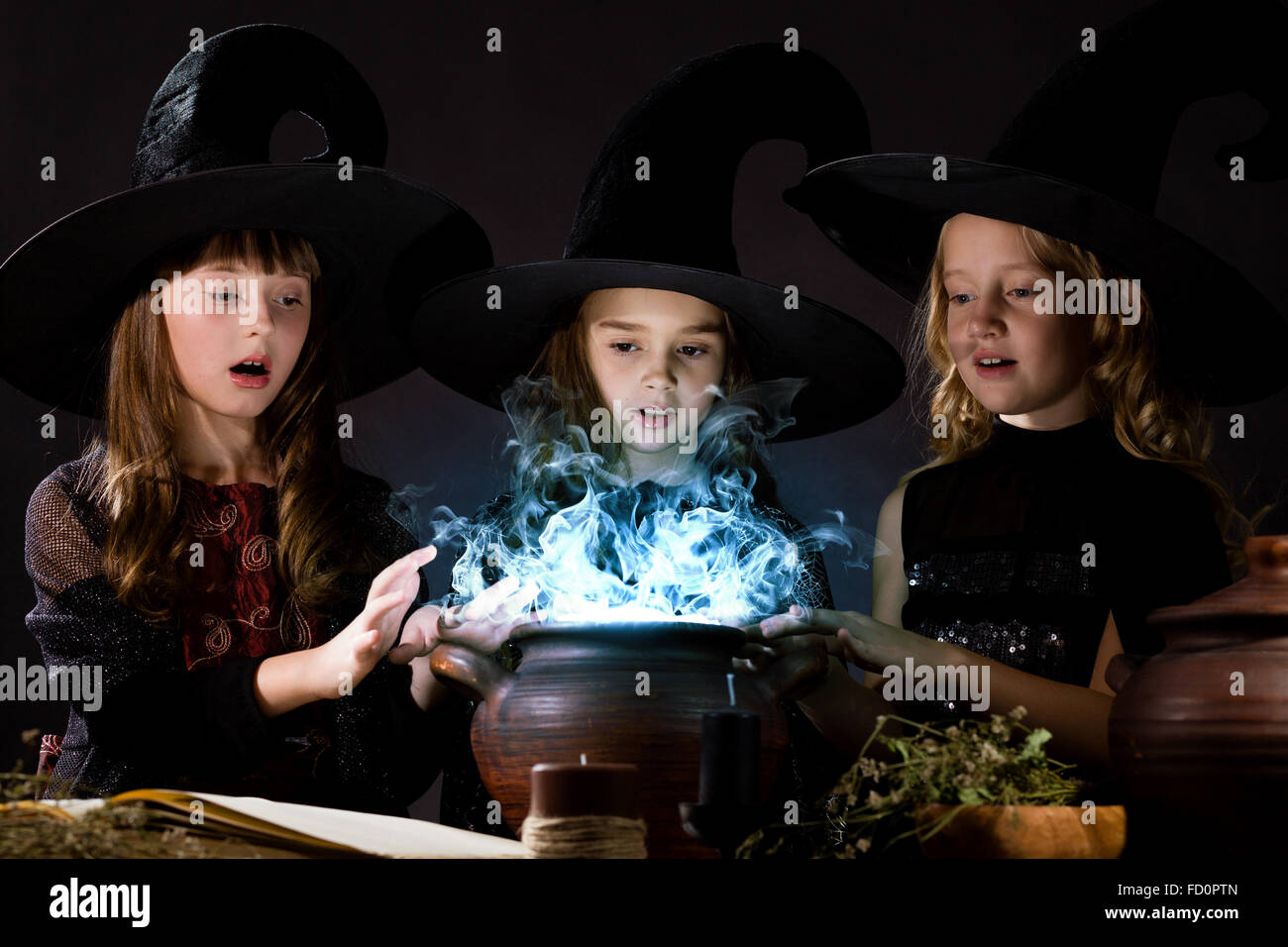 Three little Halloween witches reading spell above pot Stock Photo - Alamy