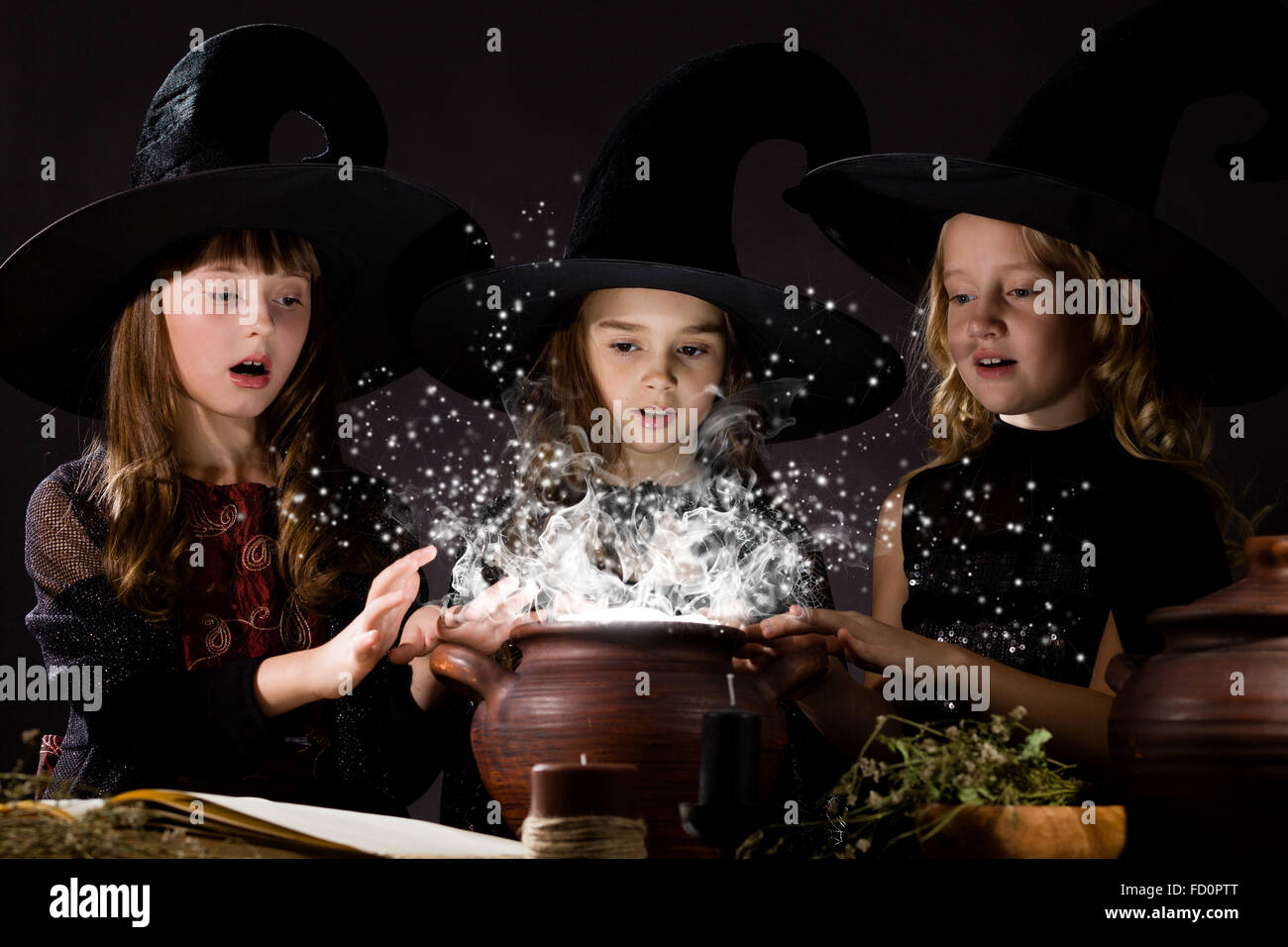 Three little Halloween witches reading spell above pot Stock Photo - Alamy