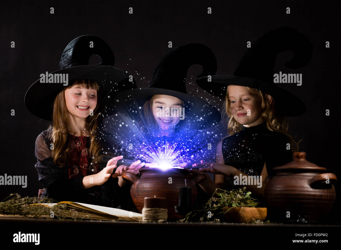 Three little Halloween witches reading spell above pot Stock Photo - Alamy