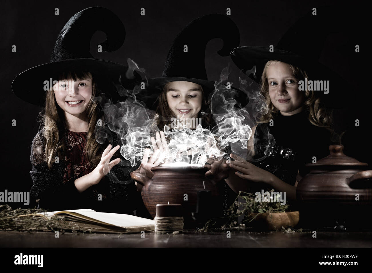 Three little Halloween witches reading spell above pot Stock Photo - Alamy