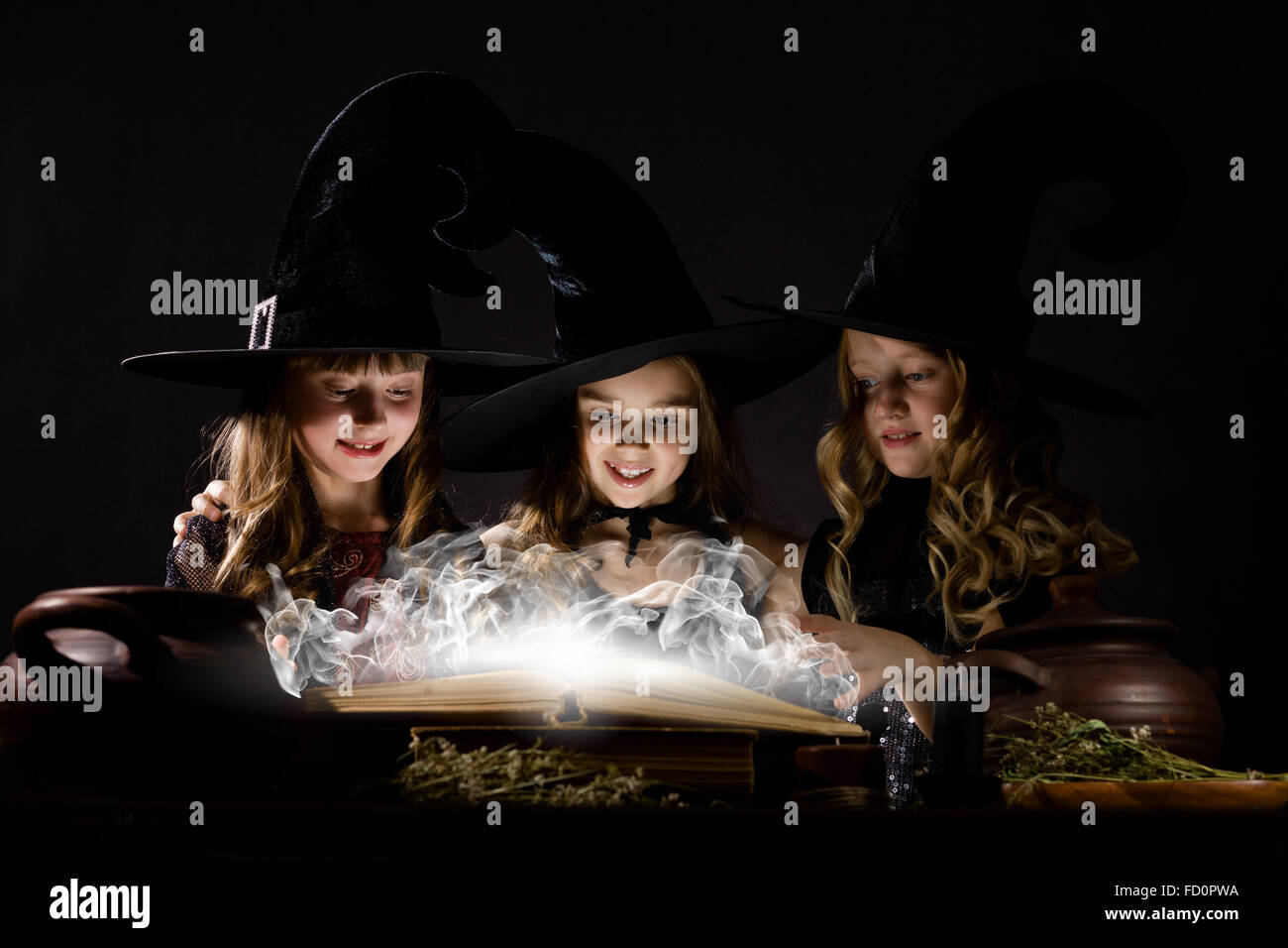 Three little Halloween witches reading spell above pot Stock Photo - Alamy