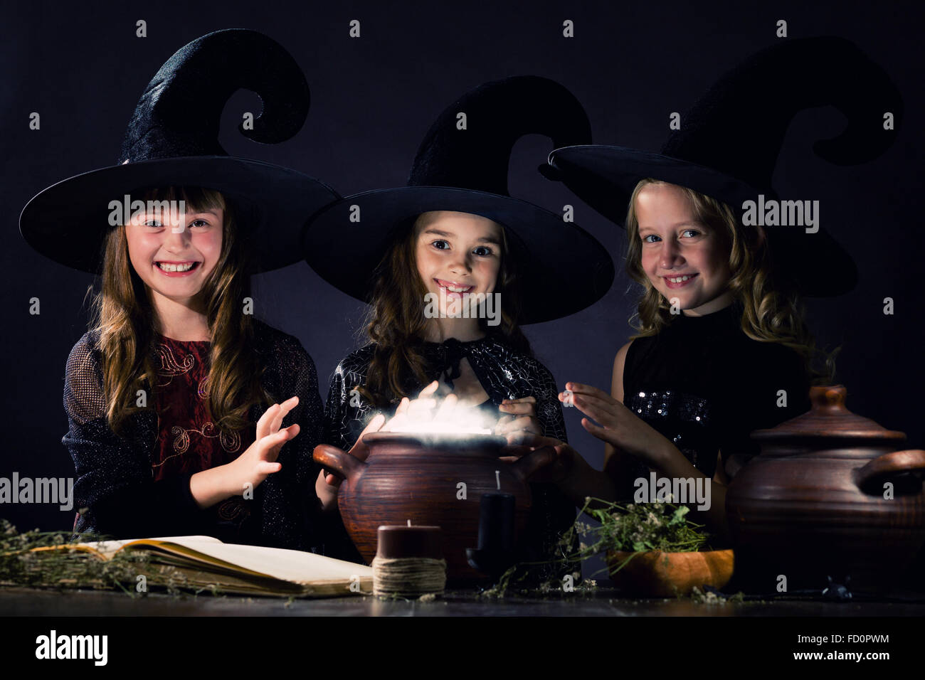 Three little Halloween witches reading spell above pot Stock Photo - Alamy