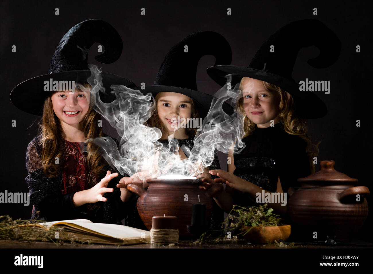 Three little Halloween witches reading spell above pot Stock Photo - Alamy
