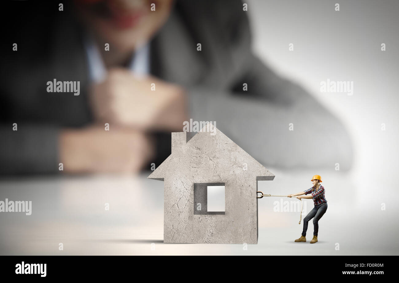 Businesswoman looking at miniature of builder pulling house model Stock ...