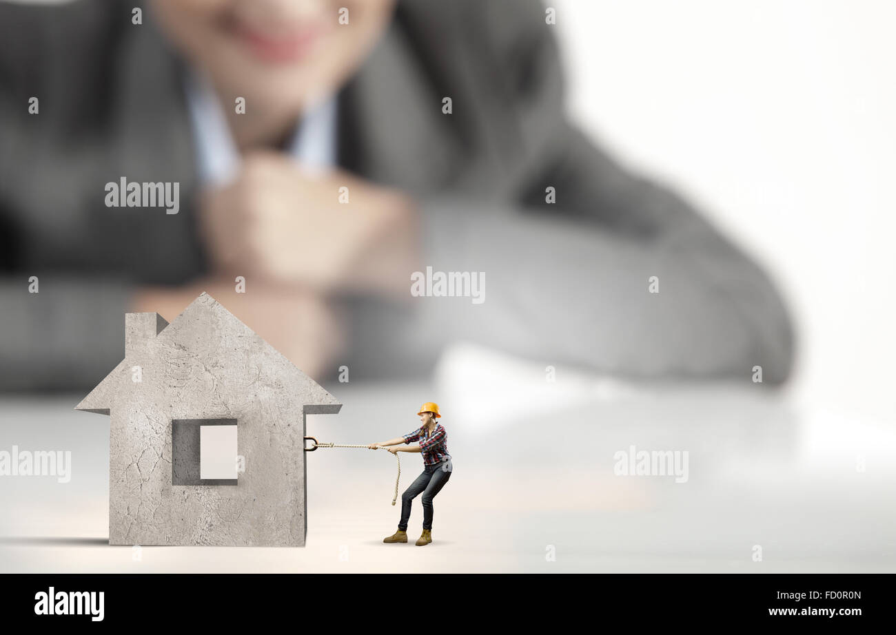 Businesswoman looking at miniature of builder pulling house model Stock ...
