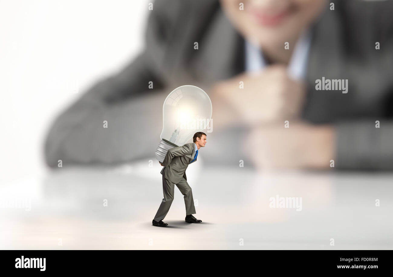 Businesswoman looking at miniature of man carrying light bulb on back ...