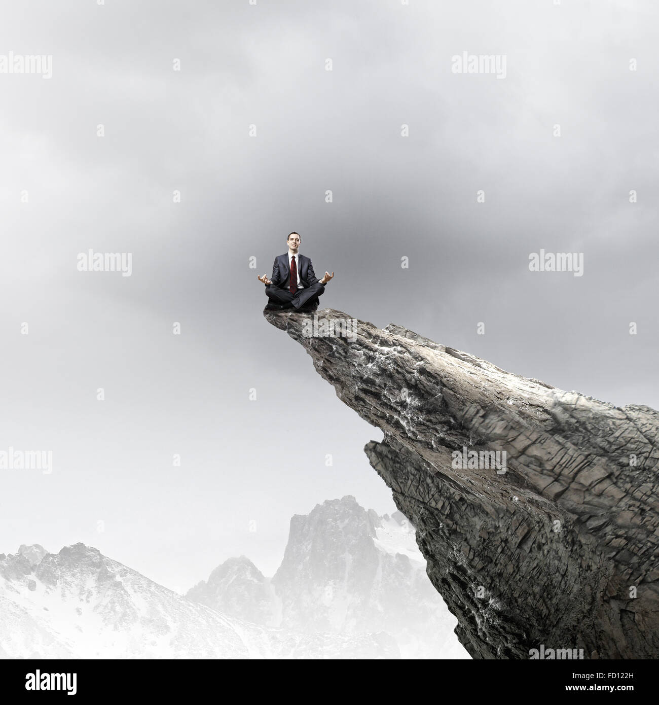 Young businessman sitting lotus pose on edge of rock mountain Stock ...