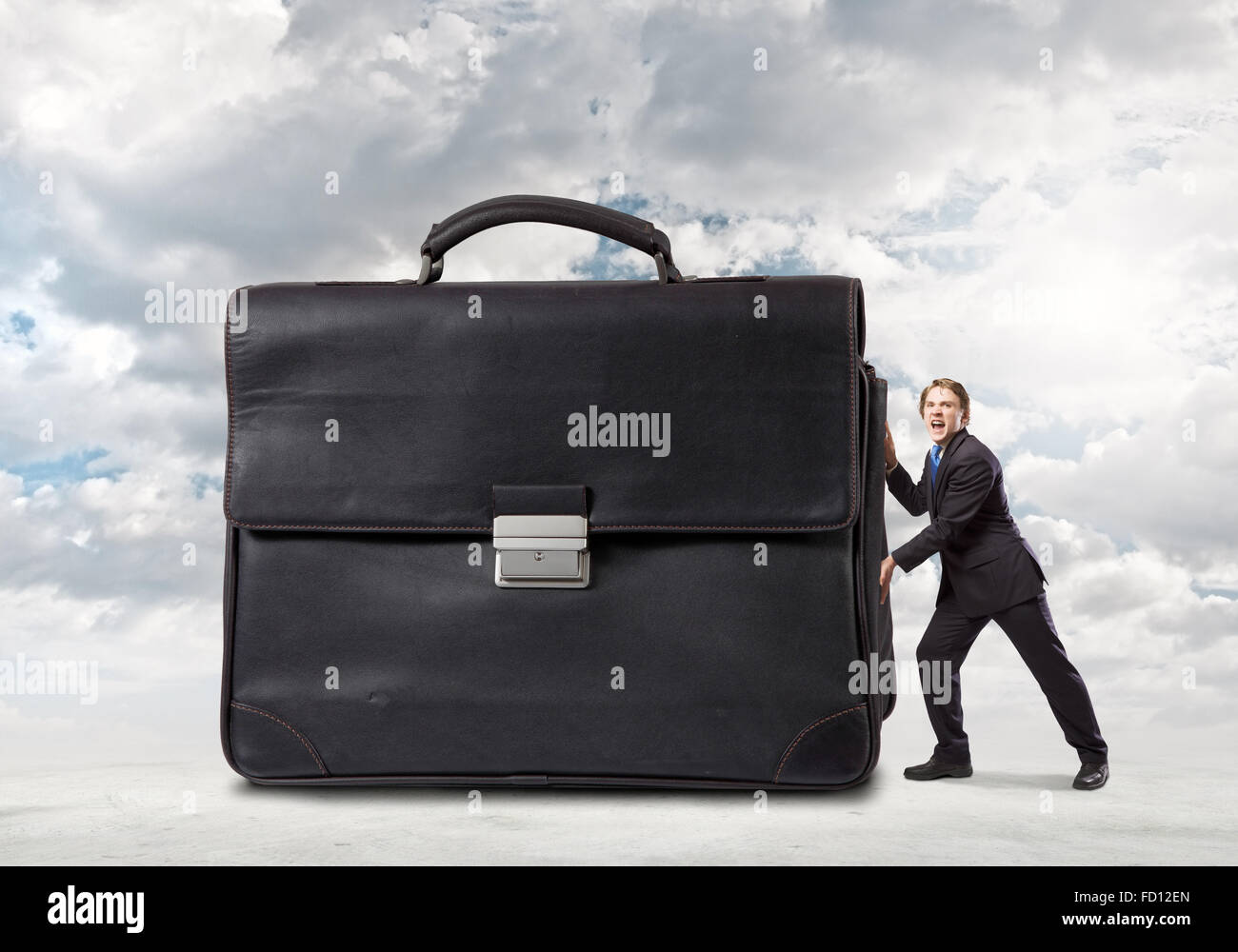 Young determined businessman pushing big heavy suitcase Stock Photo - Alamy