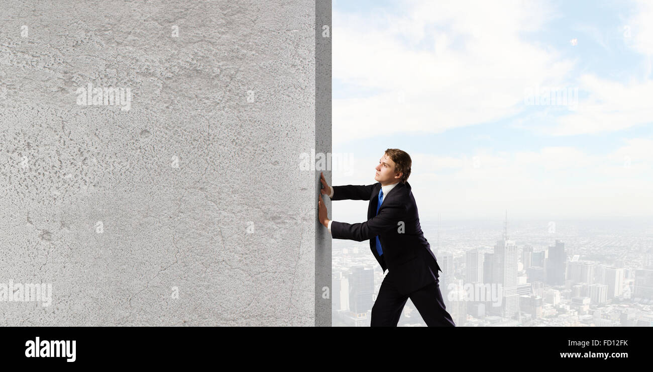 Young businessman making effort to move stone wall Stock Photo - Alamy