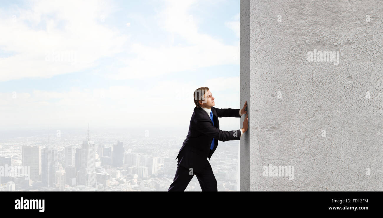 Young businessman making effort to move stone wall Stock Photo - Alamy