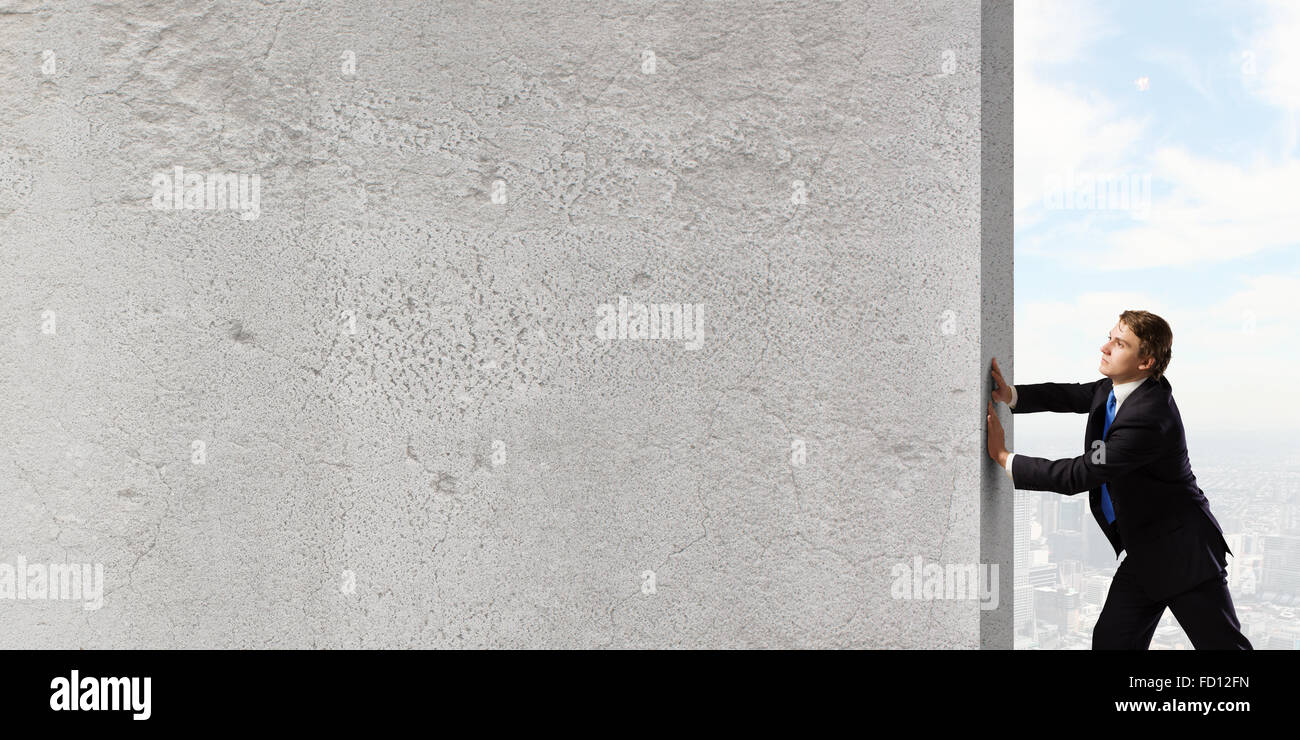 Young businessman making effort to move stone wall Stock Photo - Alamy