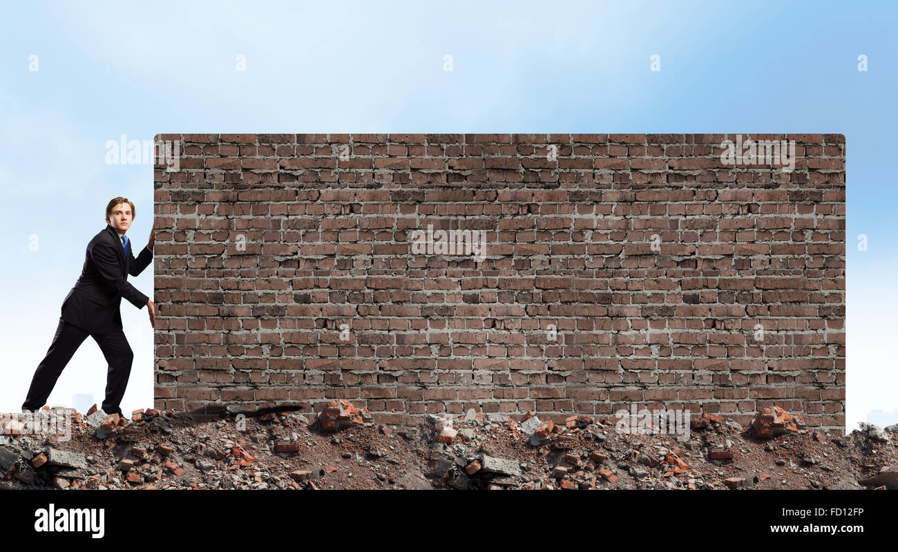 Young businessman making effort to move brick wall Stock Photo - Alamy