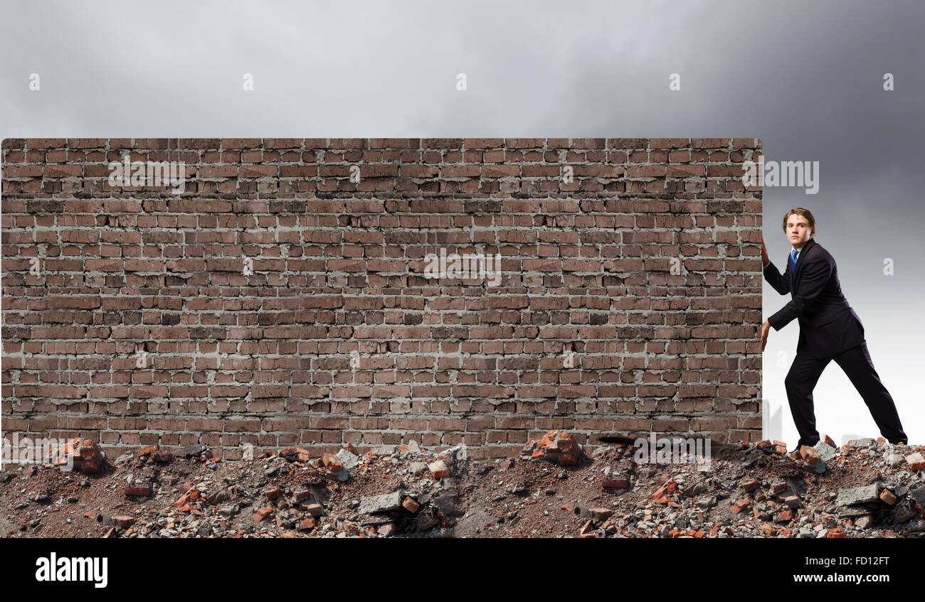 Young businessman making effort to move brick wall Stock Photo - Alamy