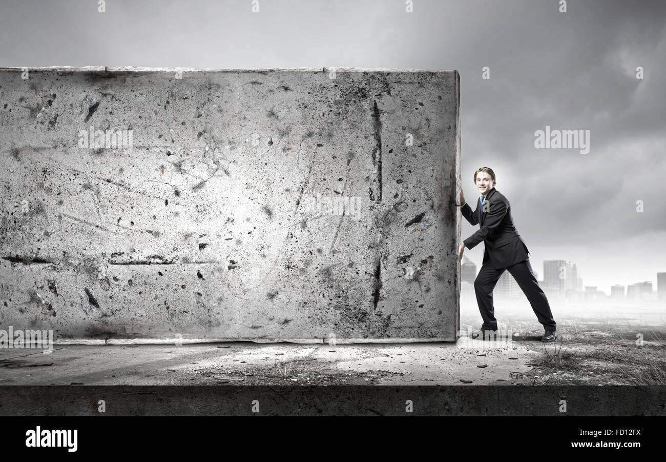 Young businessman making effort to move stone wall Stock Photo - Alamy