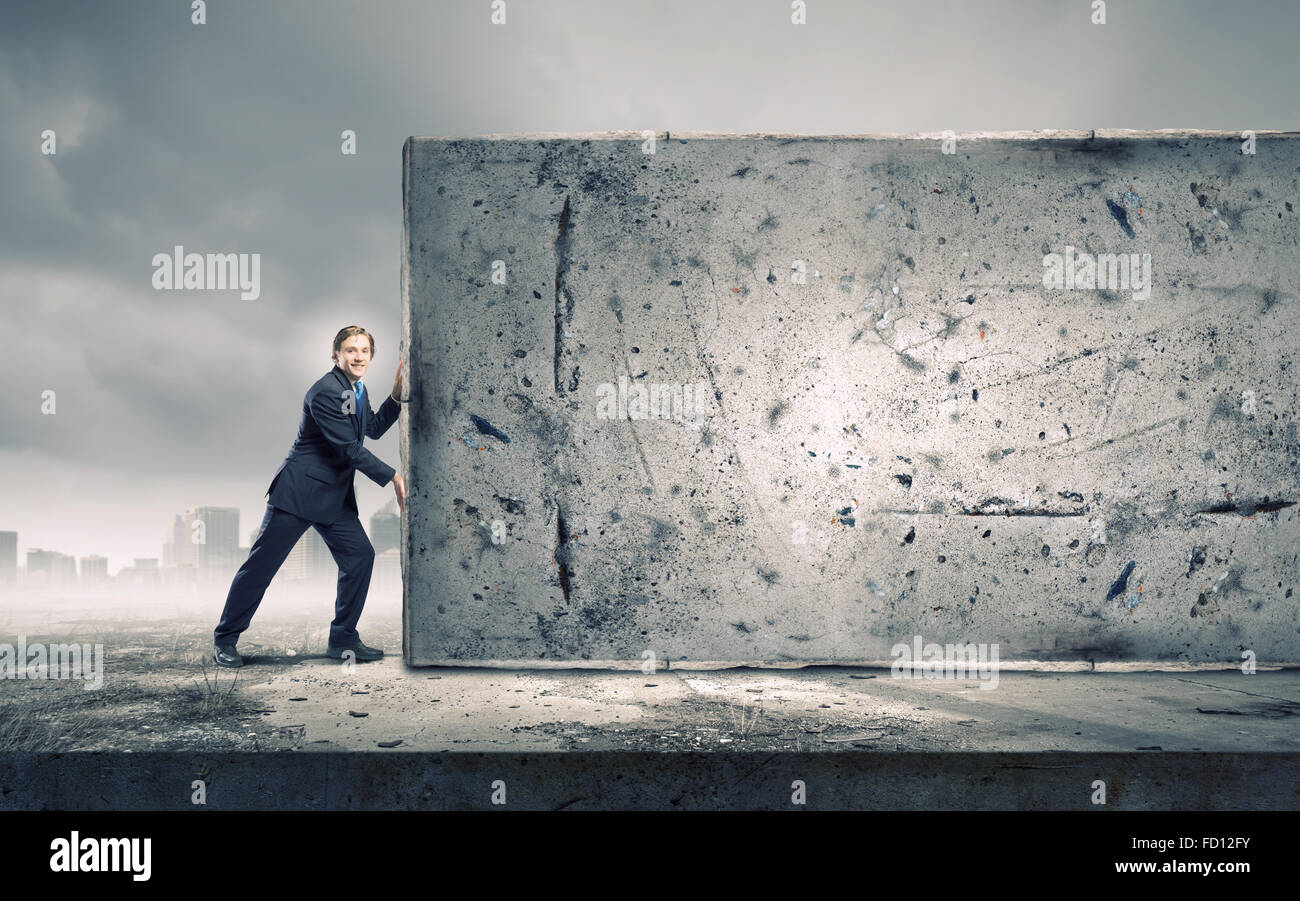 Young businessman making effort to move stone wall Stock Photo - Alamy