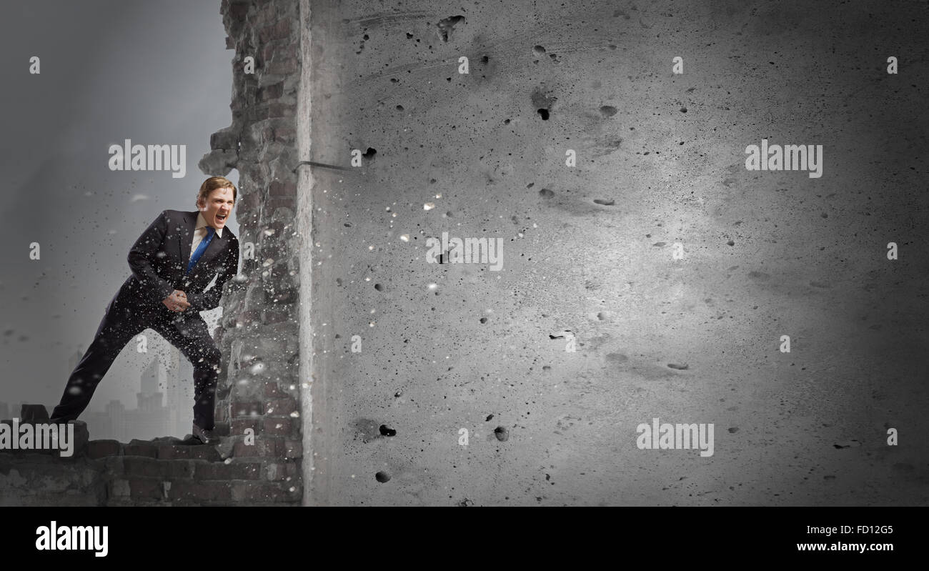 Young businessman making effort to move stone wall Stock Photo - Alamy